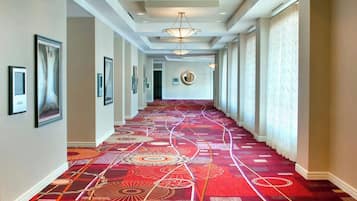 Corredor de hotel com carpete estampado, obras de arte emolduradas nas paredes e um candelabro.