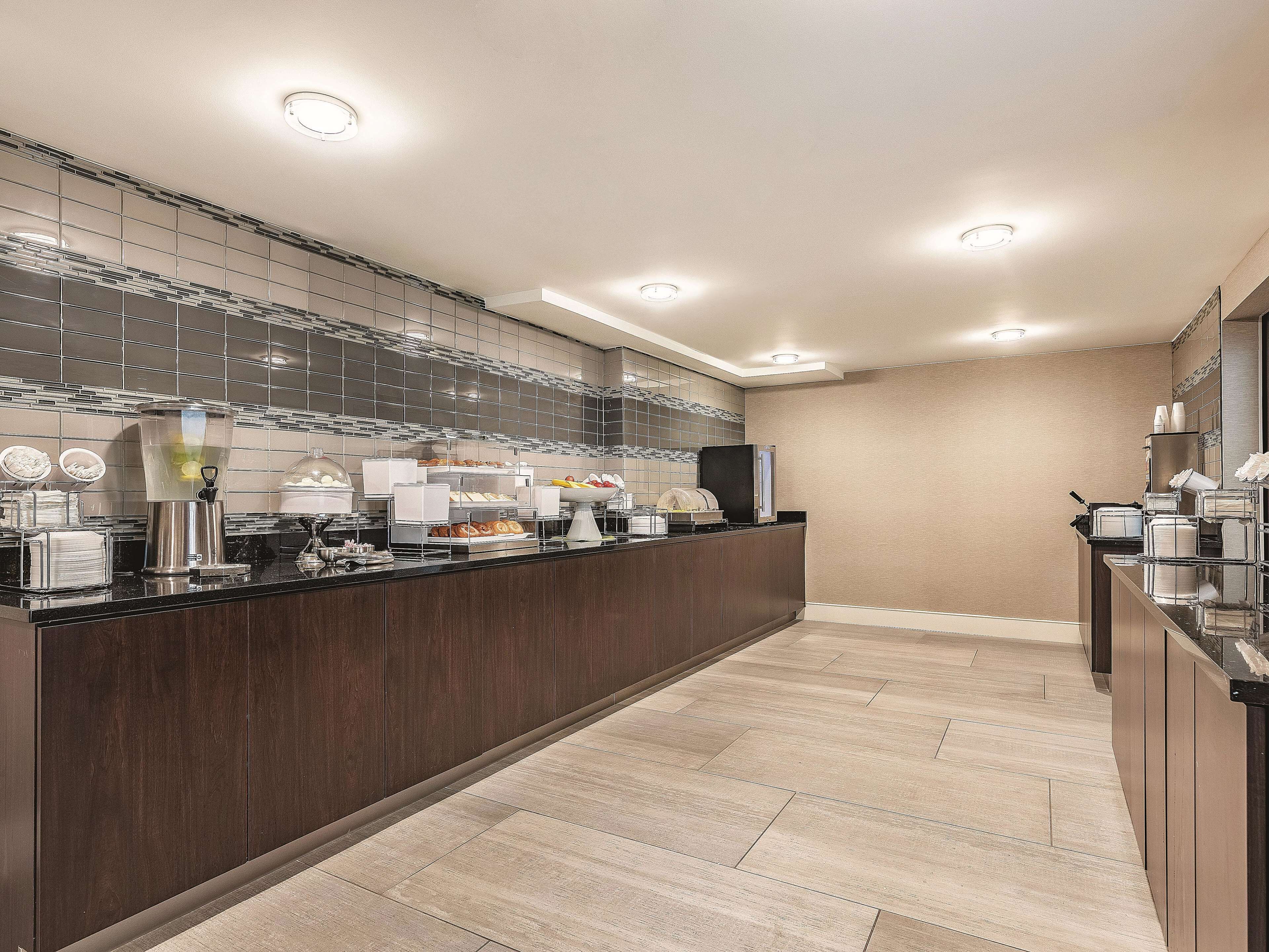Uma cozinha de hotel moderna com serviço de buffet, incluindo máquina de café, exposição de frutas e pratos organizados.