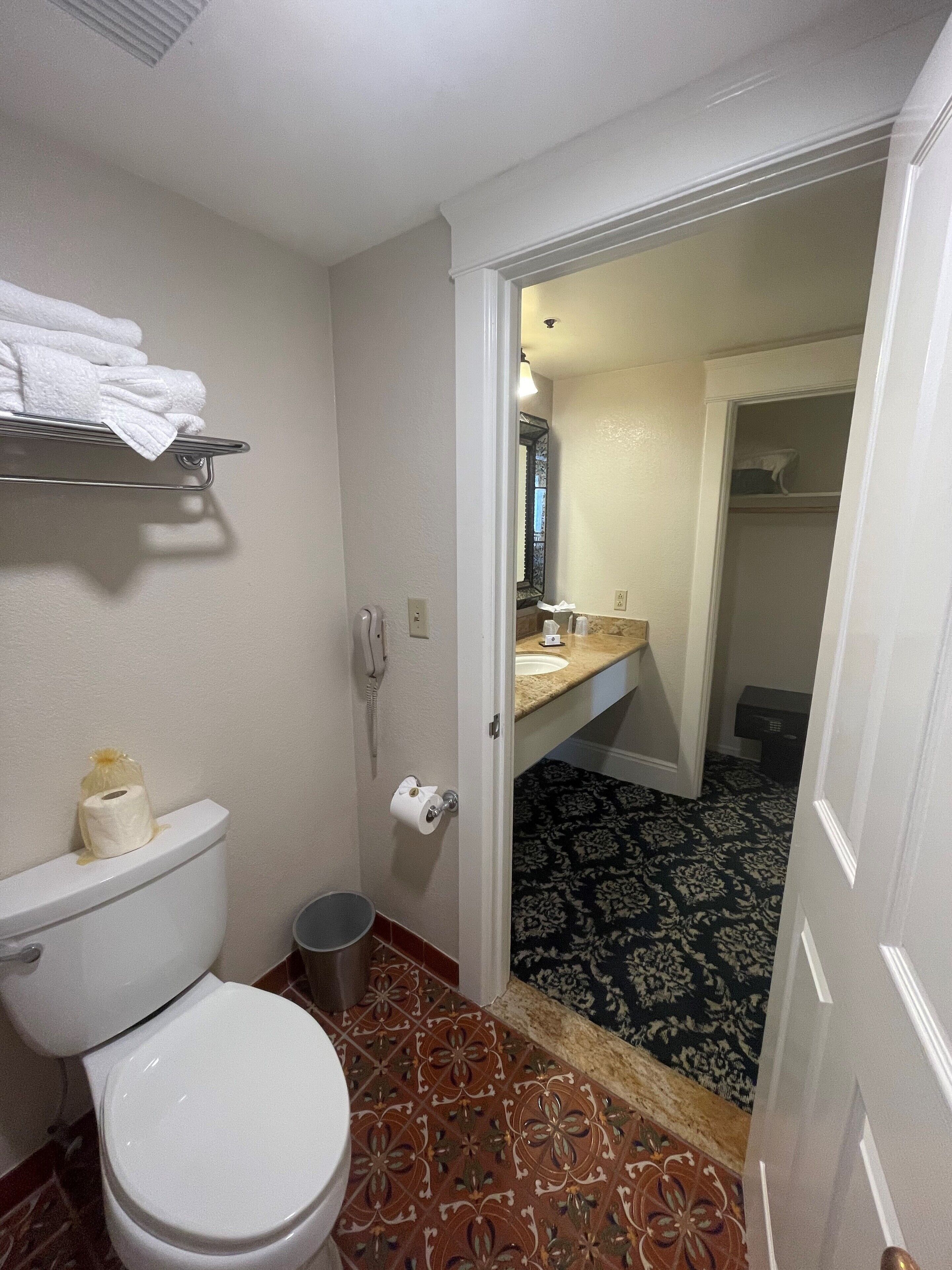 Uma casa de banho com sanita, um porta-toalhas, um suporte para papel higiénico e um cesto de lixo.