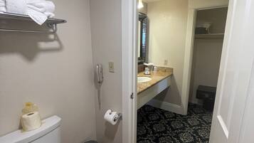 Uma casa de banho com sanita, um porta-toalhas, um suporte para papel higiénico e um cesto de lixo.