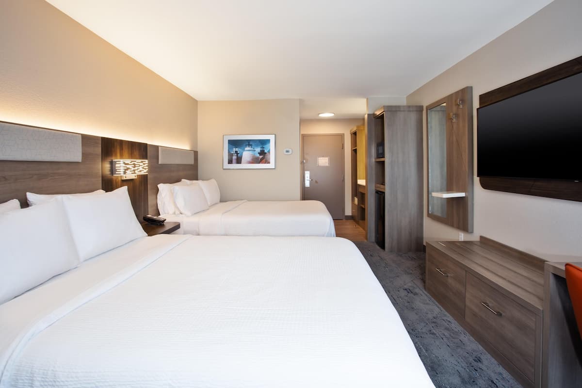 Quarto de hotel com duas camas, uma televisão de tela plana, um aparador de madeira e um quadro na parede.