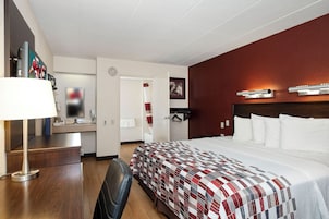 Quarto de hotel com cama, escrivaninha, cadeira, televisão e banheiro visível por uma porta aberta.