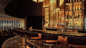 Uma área de bar com balcão curvo, vários bancos e um expositor bem iluminado com garrafas.