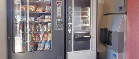 Máquina de vendas com diversas opções de lanches e uma pequena geladeira com um adesivo azul.