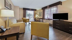 Quarto de hotel com sofá, poltrona, escrivaninha com luminária, televisão e cómoda.