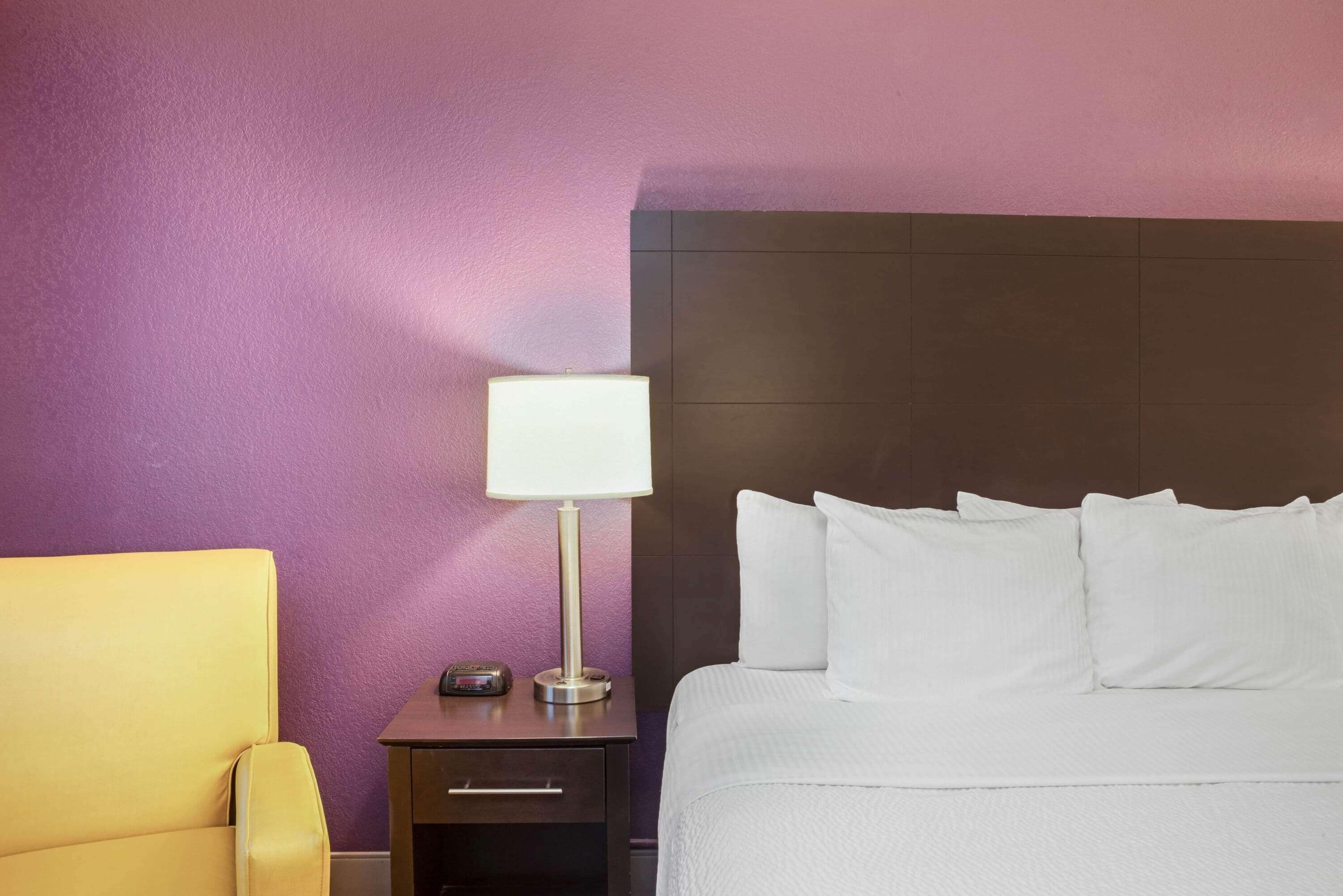 Quarto de hotel com cama, mesa de cabeceira com abajur e uma cadeira.