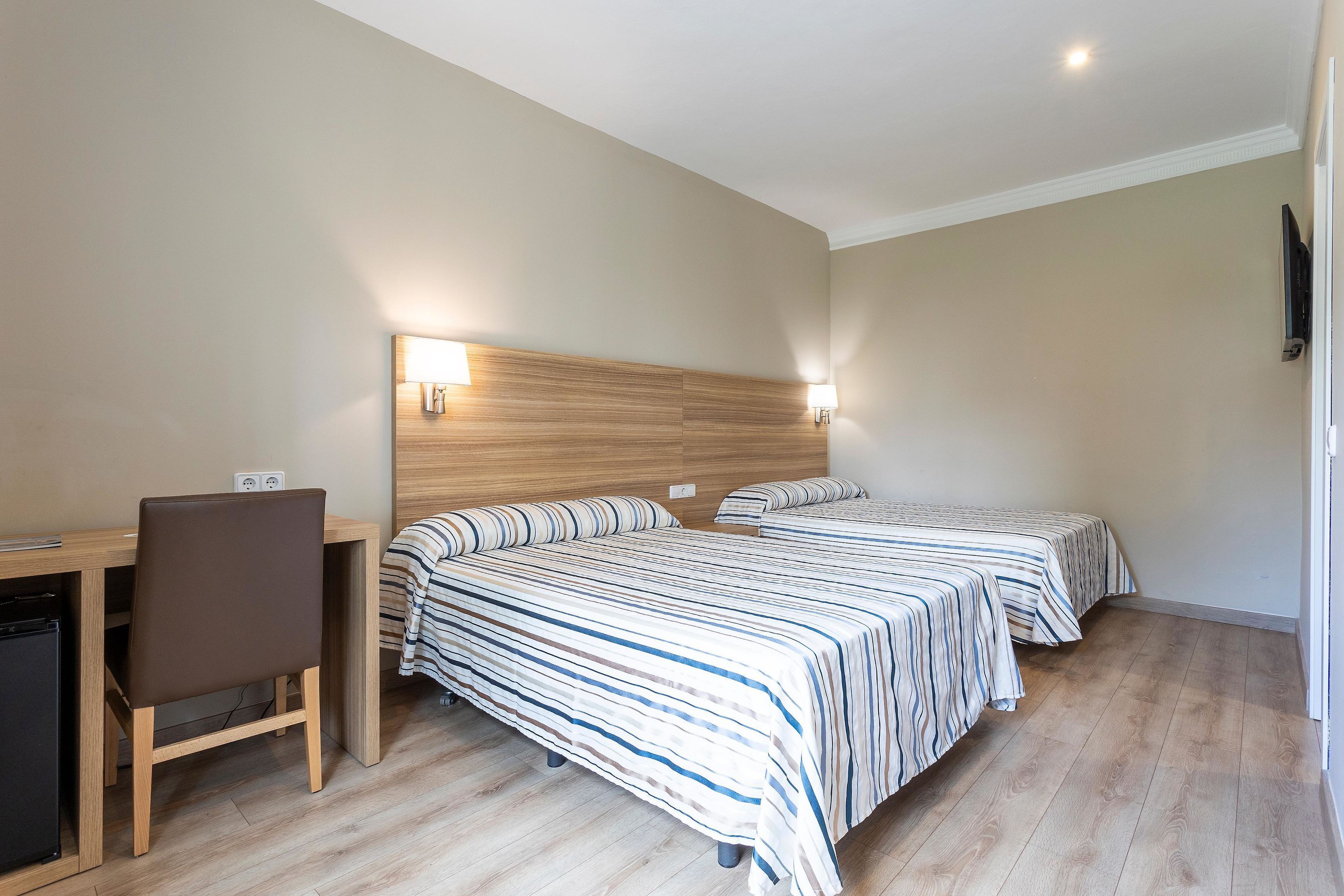 Quarto de hotel com duas camas, uma escrivaninha e uma cadeira.