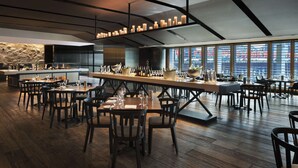 Um restaurante moderno com uma mesa comunitária grande, assentos individuais e janelas amplas com vista para a paisagem urbana.