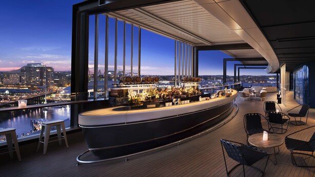 Um bar à beira-mar com vista para a cidade, deck de madeira e assentos modernos.
