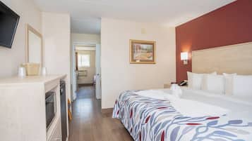 Quarto de hotel com uma cama, uma escrivaninha, uma televisão e um quadro na parede.