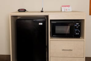 Uma cozinha compacta com geladeira preta, micro-ondas e um relógio na bancada.