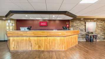 Uma mesa de recepção com uma placa indicando 'Wi-Fi Gratuito em Todos os Quartos', uma parede de pedra e uma placa da 'Red Roof Inn'.