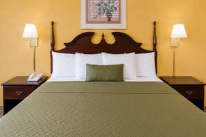 Quarto de hotel com uma cama grande, duas mesas de cabeceira, um telefone e duas luminárias fixadas na parede.