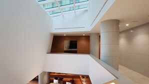 Um interior moderno com teto de vidro, escada e área de estar com mesas e cadeiras.