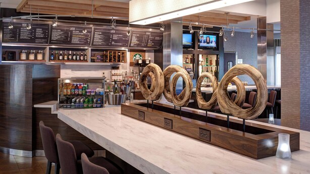 Uma área de bar moderna com um balcão comprido, vários taburetes e uma seleção de garrafas e copos.