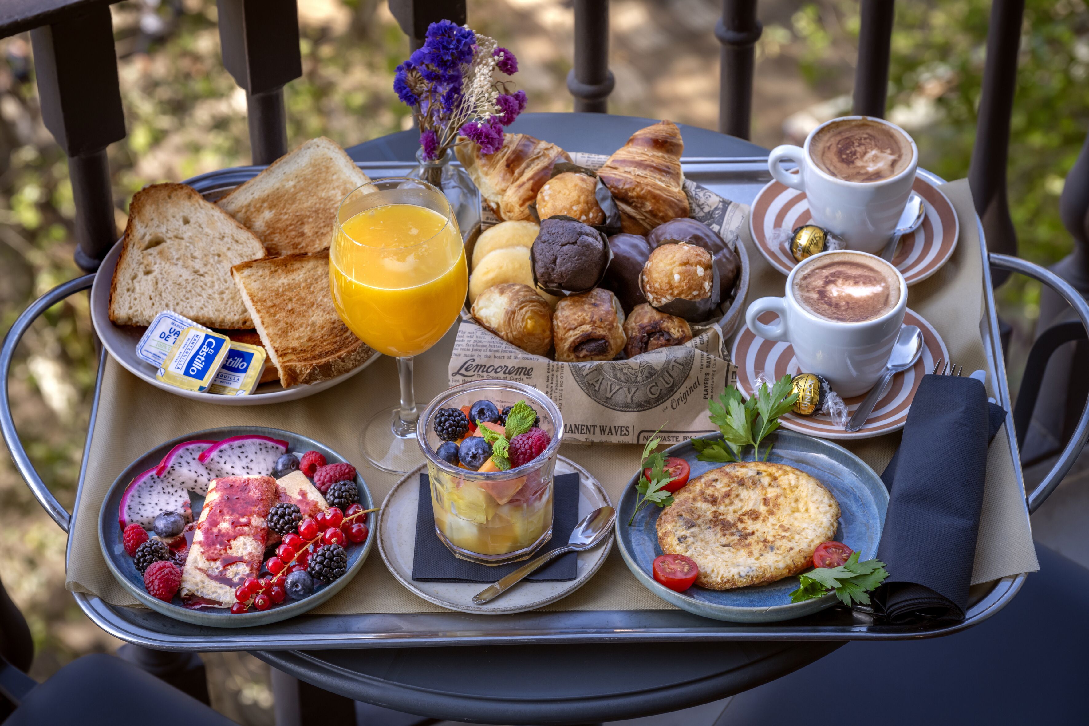 Uma bandeja com itens de café da manhã, incluindo torradas, croissants, doces, frutas e bebidas.