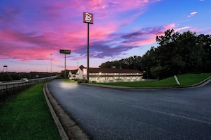 Um Red Roof Inn com uma grande placa, localizado ao lado de uma rodovia com área gramada e árvores.