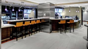 Uma área de bar moderna com várias opções de assento, balcão de aço inoxidável e iluminação pendente.