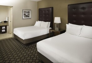 Quarto de hotel com duas camas, uma mesa de cabeceira com abajur, um quadro na parede e um tapete estampado.