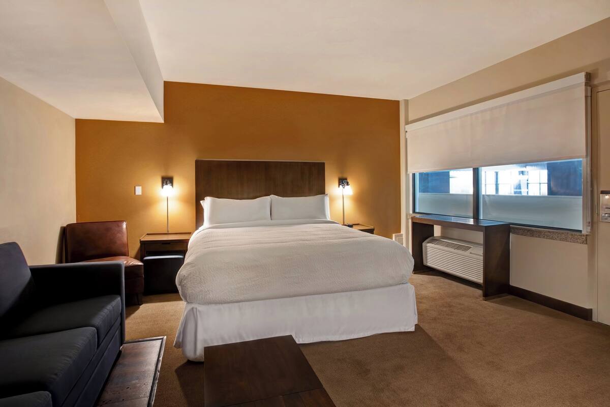 Quarto de hotel com uma cama grande, duas luminárias de cabeceira, uma TV, uma escrivaninha e uma cadeira.