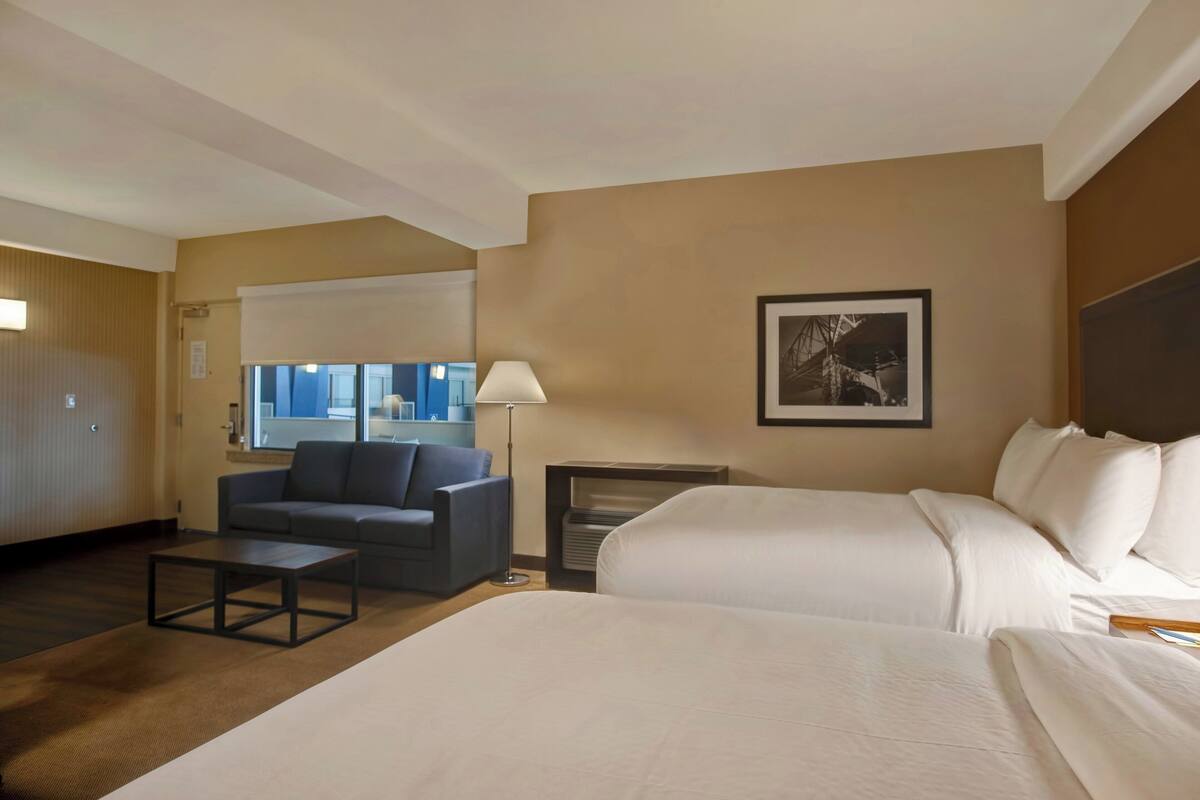 Quarto de hotel com uma cama grande, um sofá, uma mesa de centro, uma luminária e um quadro na parede.