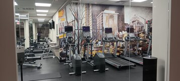 Uma academia com diversos equipamentos de exercício, incluindo esteiras e aparelhos de musculação, e um mural na parede.