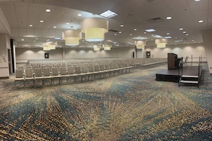 Uma sala de conferências com fileiras de cadeiras, um palco e piso coberto de carpete.