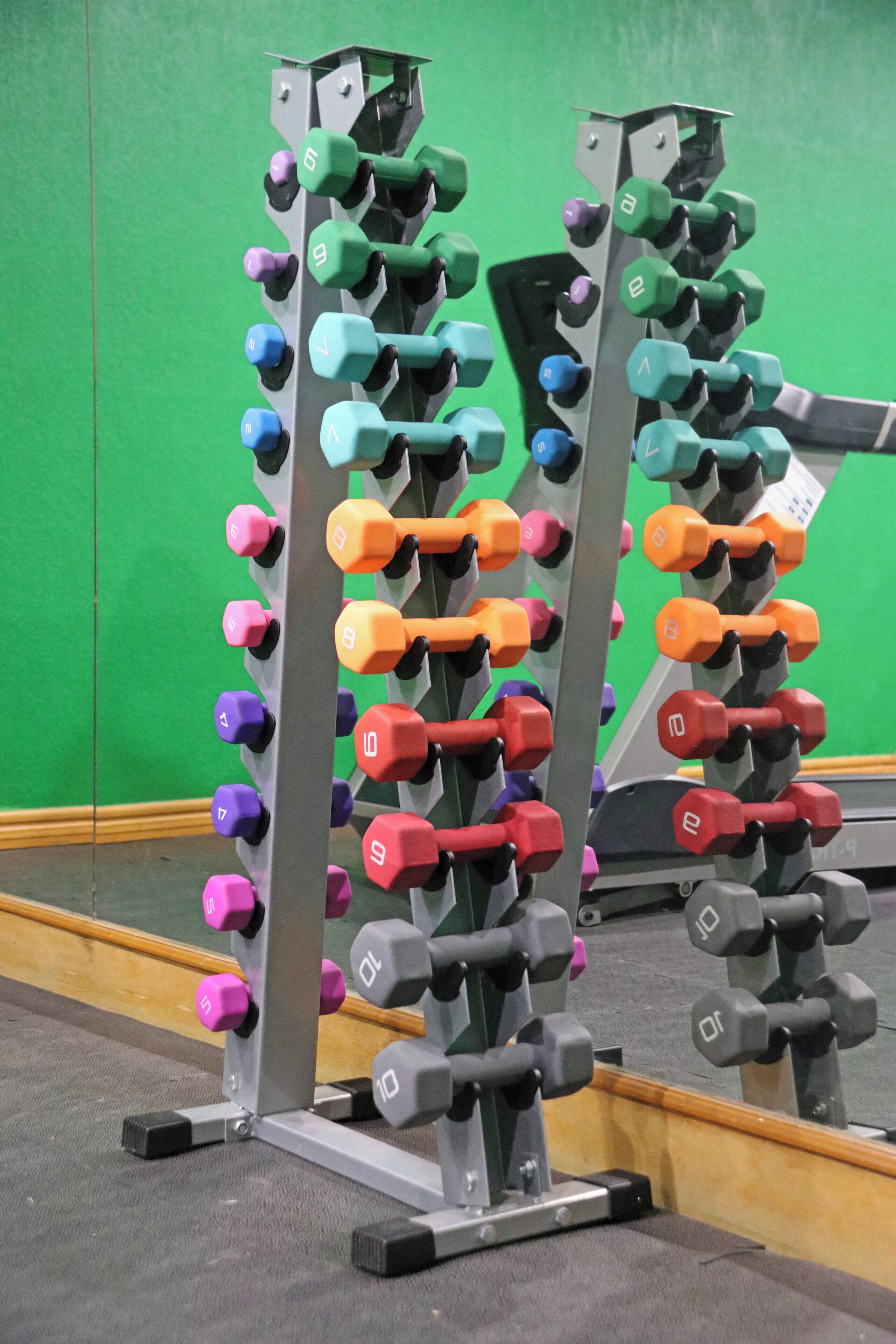 Uma academia com várias fileiras de equipamentos de musculação, incluindo halteres e barras.