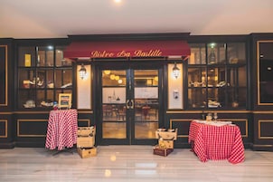 Exterior do Bistro La Bastille com toldo vermelho, portas de vidro e mesas montadas ao ar livre com toalhas de xadrez e caixas de vinho.