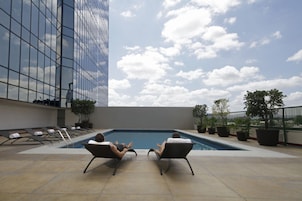 Uma área de piscina no terraço com duas espreguiçadeiras, uma piscina e plantas em vasos.