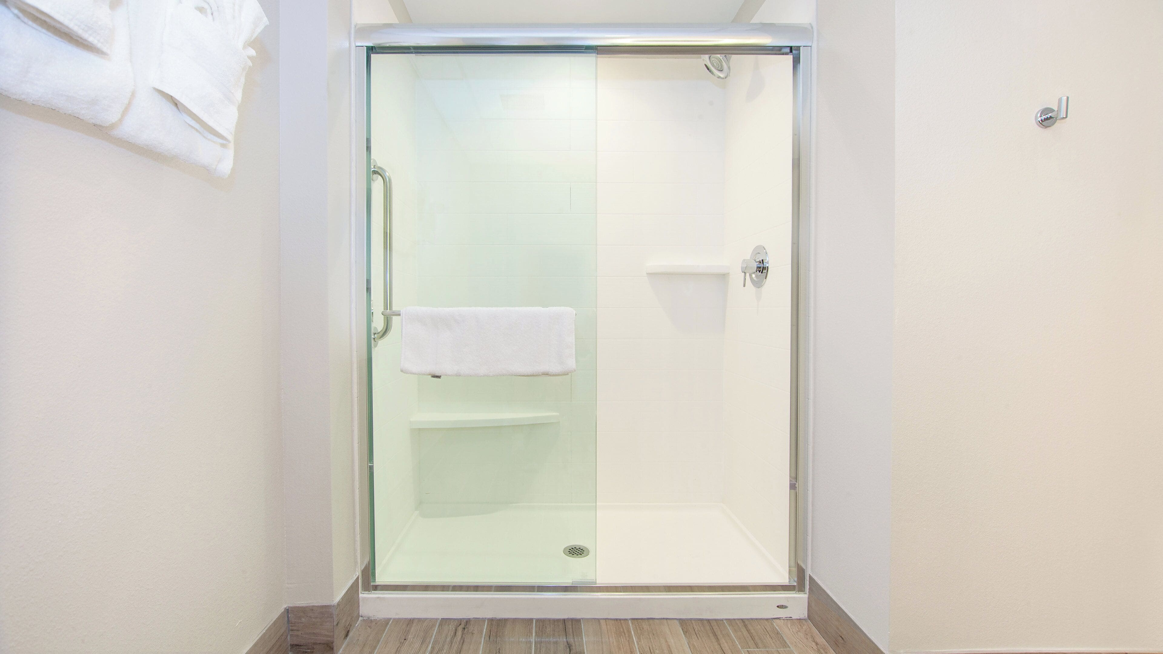 Um chuveiro com paredes de vidro, uma toalha branca em um porta-toalhas, uma porta de vidro e um revestimento de azulejos brancos.