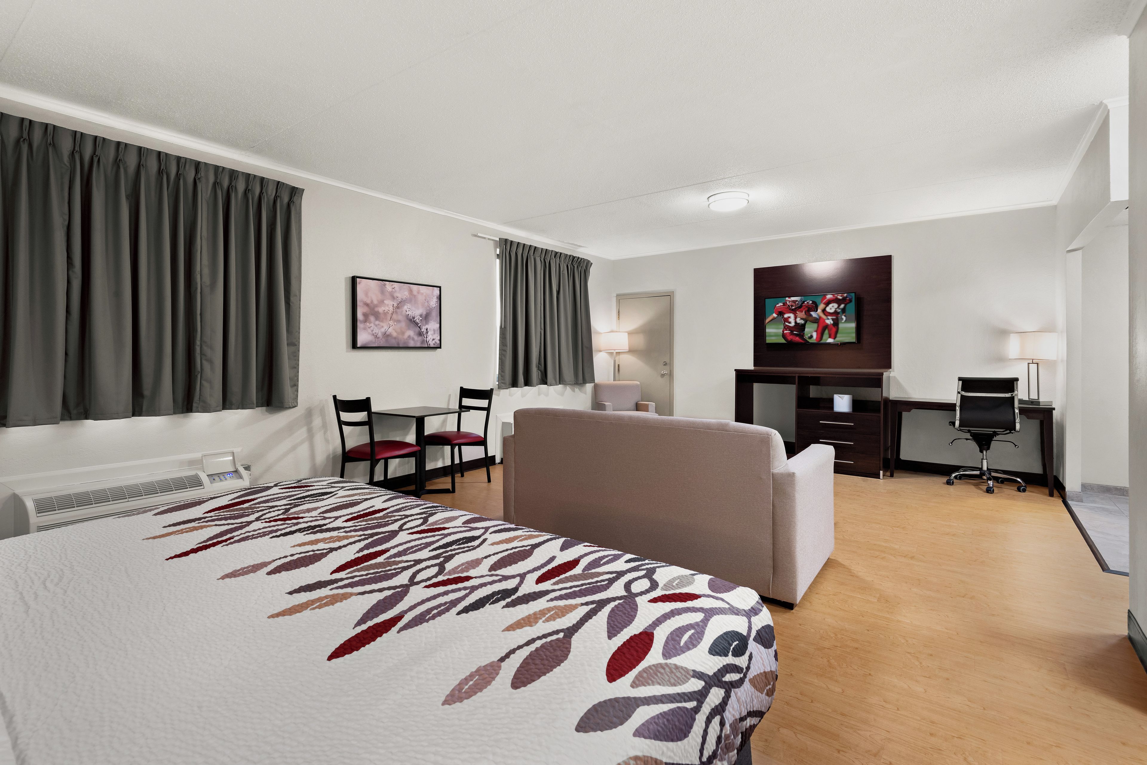 Quarto de hotel com cama, escrivaninha, cadeira, televisão e janela com cortinas.