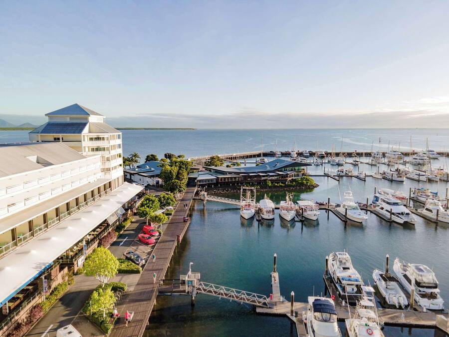 Marina com vários barcos atracados, uma ponte para pedestres e um edifício grande com telhado azul.