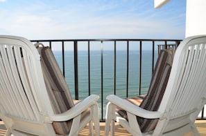 Duas cadeiras brancas com almofadas listradas viradas para uma varanda com vista para o mar.