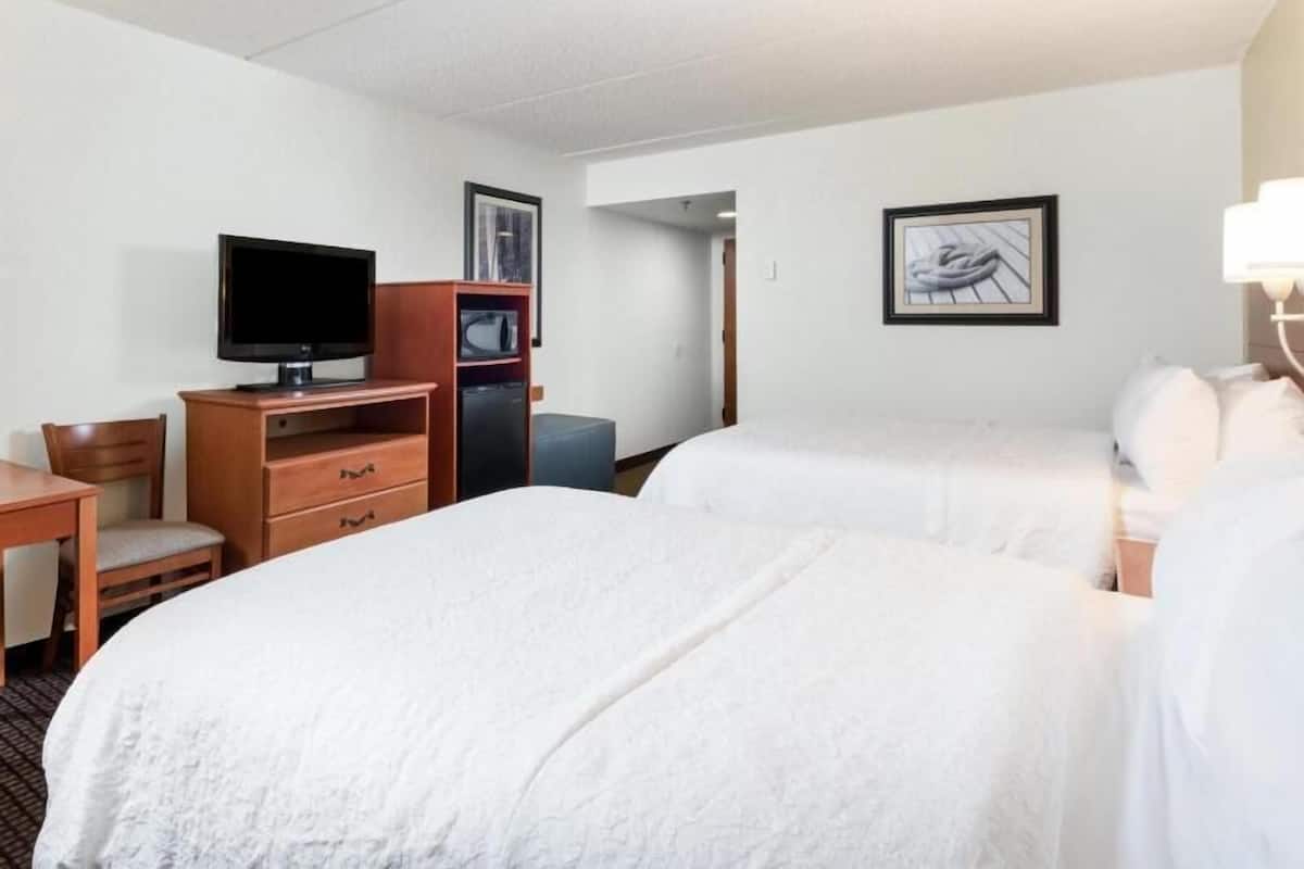 Quarto de hotel com duas camas, uma mesa de trabalho com televisão, um frigorífico pequeno e uma cadeira.