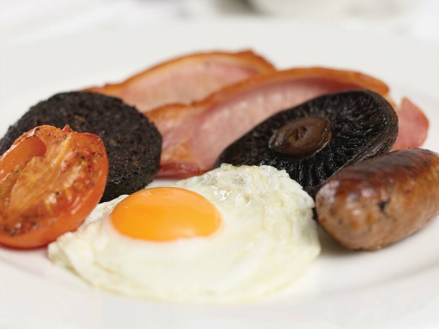 Prato de comida de café da manhã com ovos, salsichas, bacon e tomates.