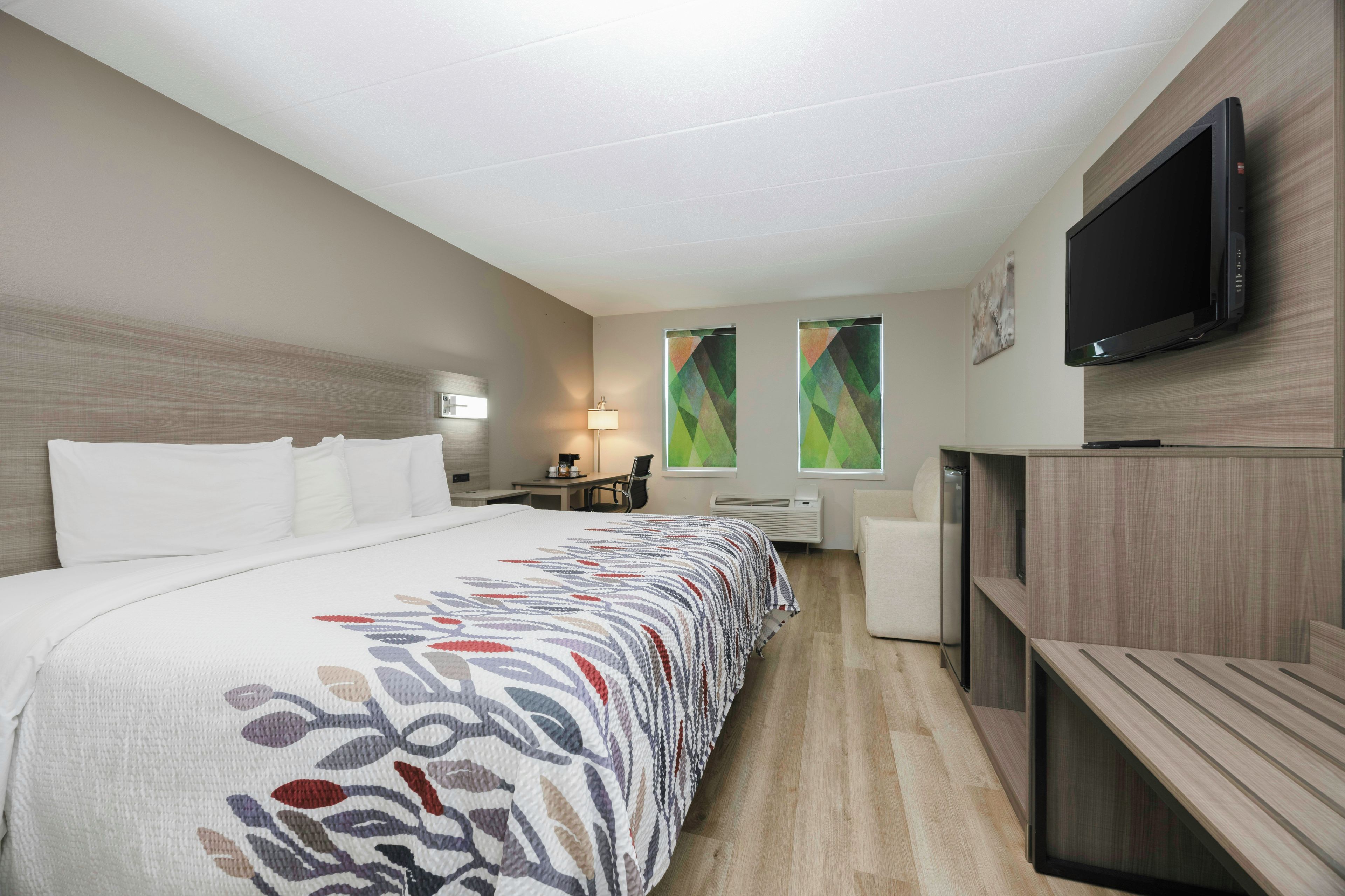Quarto de hotel com uma cama grande, uma escrivaninha, uma cadeira, uma televisão e duas janelas com obras de arte.