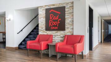 Um saguão de hotel com uma escada, duas cadeiras vermelhas e uma placa fixada na parede com a inscrição 'Red Roof Inn'.