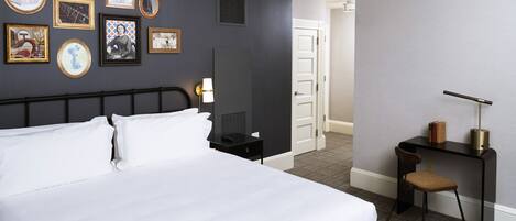 Quarto de hotel com uma cama grande, uma mesa de trabalho com cadeira e parede decorada com quadros.
