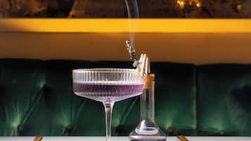 Um copo de cocktail sobre um apoio, com uma garrafa e um cachimbo de água.