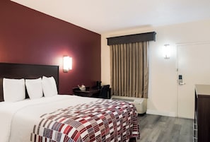Quarto de hotel com cama, escrivaninha, cadeira, guarda-roupa e janela com cortinas.