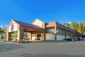 Hotel com entrada coberta, estacionamento e céu azul.