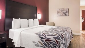Quarto de hotel com uma cama grande, cabeceira escura, luminária na parede e um quadro.
