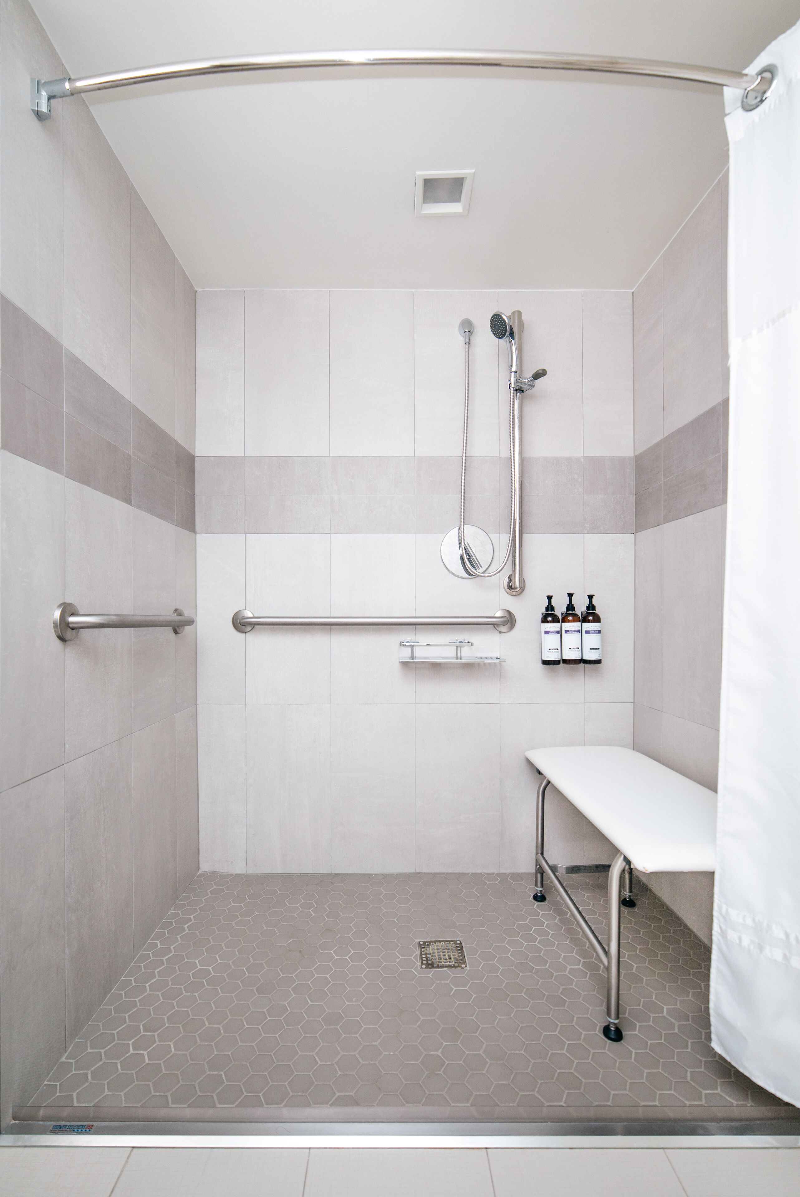 Área de duche com barra de apoio, banco e prateleira com produtos de higiene pessoal.