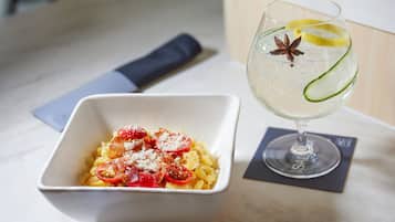 Uma tigela branca com massa, tomate cereja e um copo de água com rodelas de limão e uma estrela-anis.