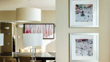 Quarto de hotel com área de refeições, uma janela grande e duas fotografias emolduradas na parede.
