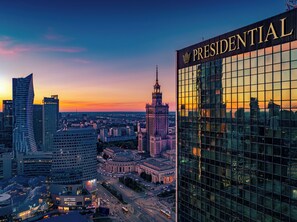 Paisagem urbana com edifícios modernos e históricos, incluindo uma torre do relógio imponente e um edifício com a inscrição 'PRESIDENTIAL'.