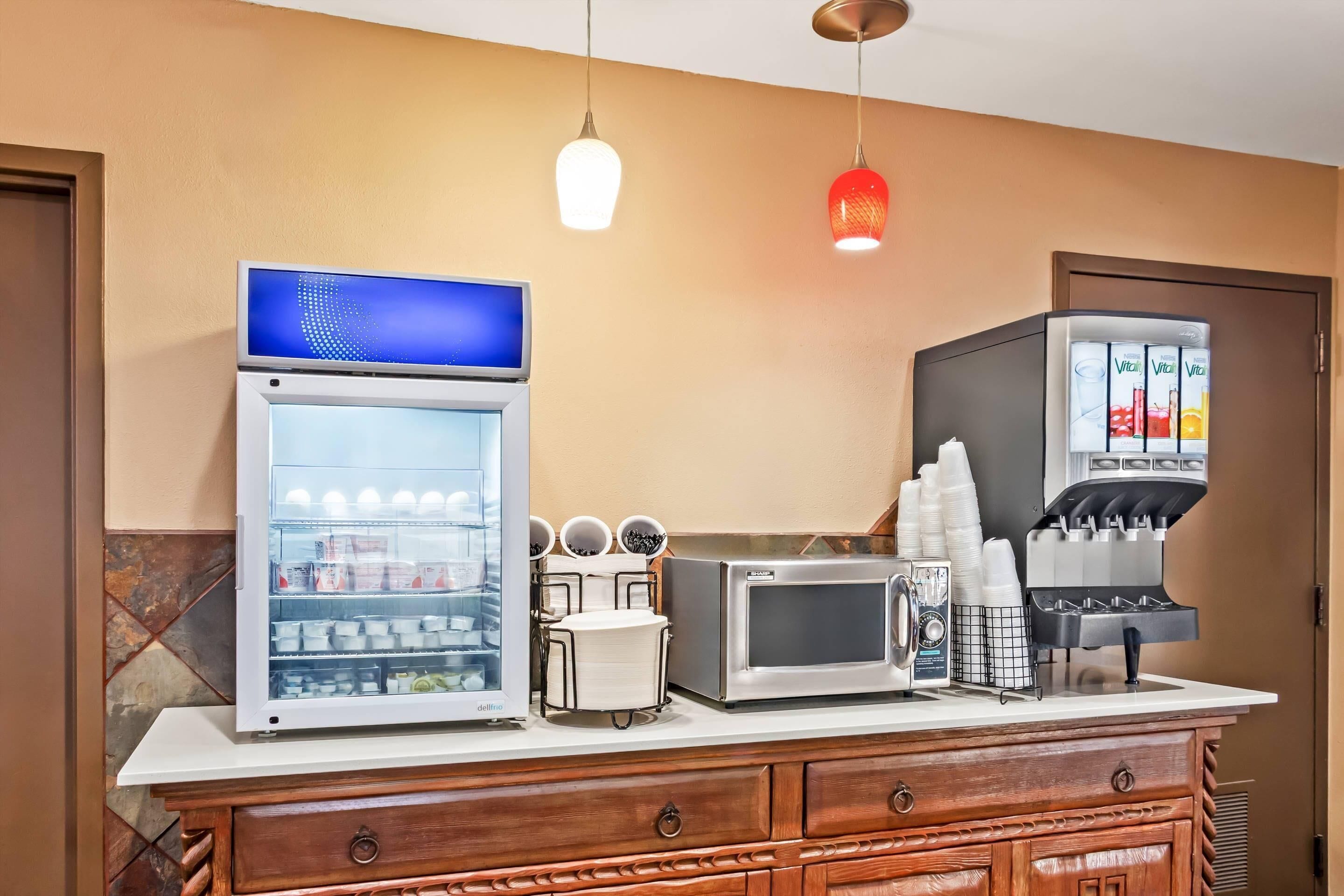Uma cozinha compacta equipada com geladeira, micro-ondas, máquina de café e dispensador de bebidas.