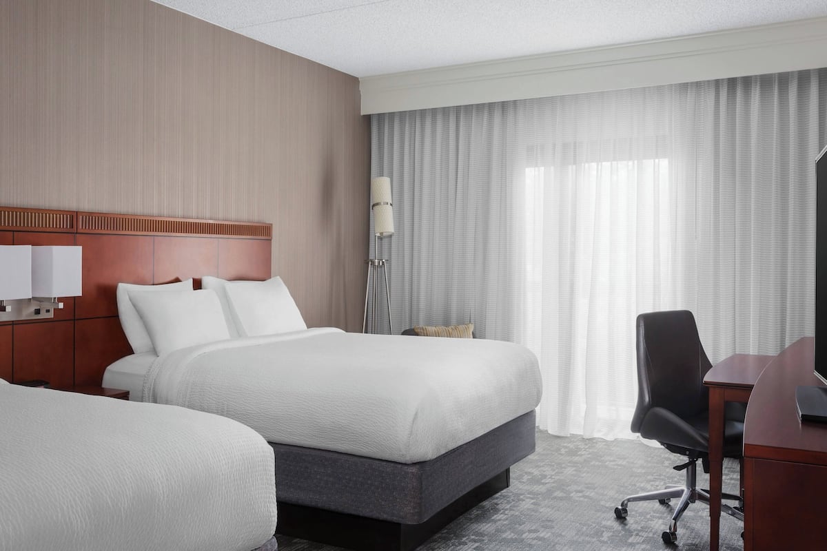 Quarto de hotel com duas camas, uma escrivaninha e uma cadeira.