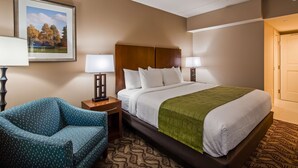 Quarto de hotel com uma cama, duas luminárias de cabeceira, uma cadeira e um quadro na parede.